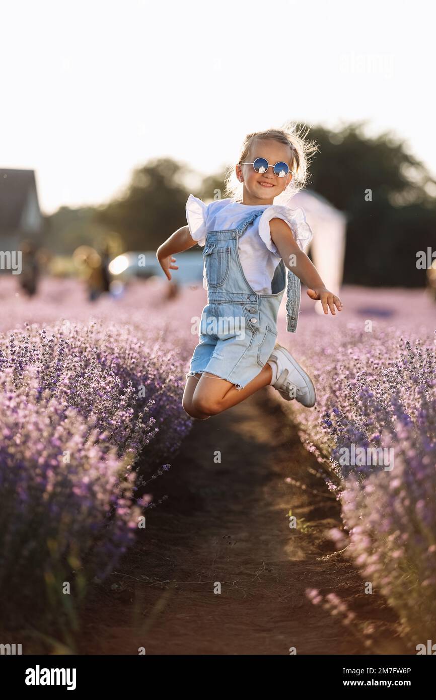 Adorable happy child girl is having fun and jumping in lavender field ...