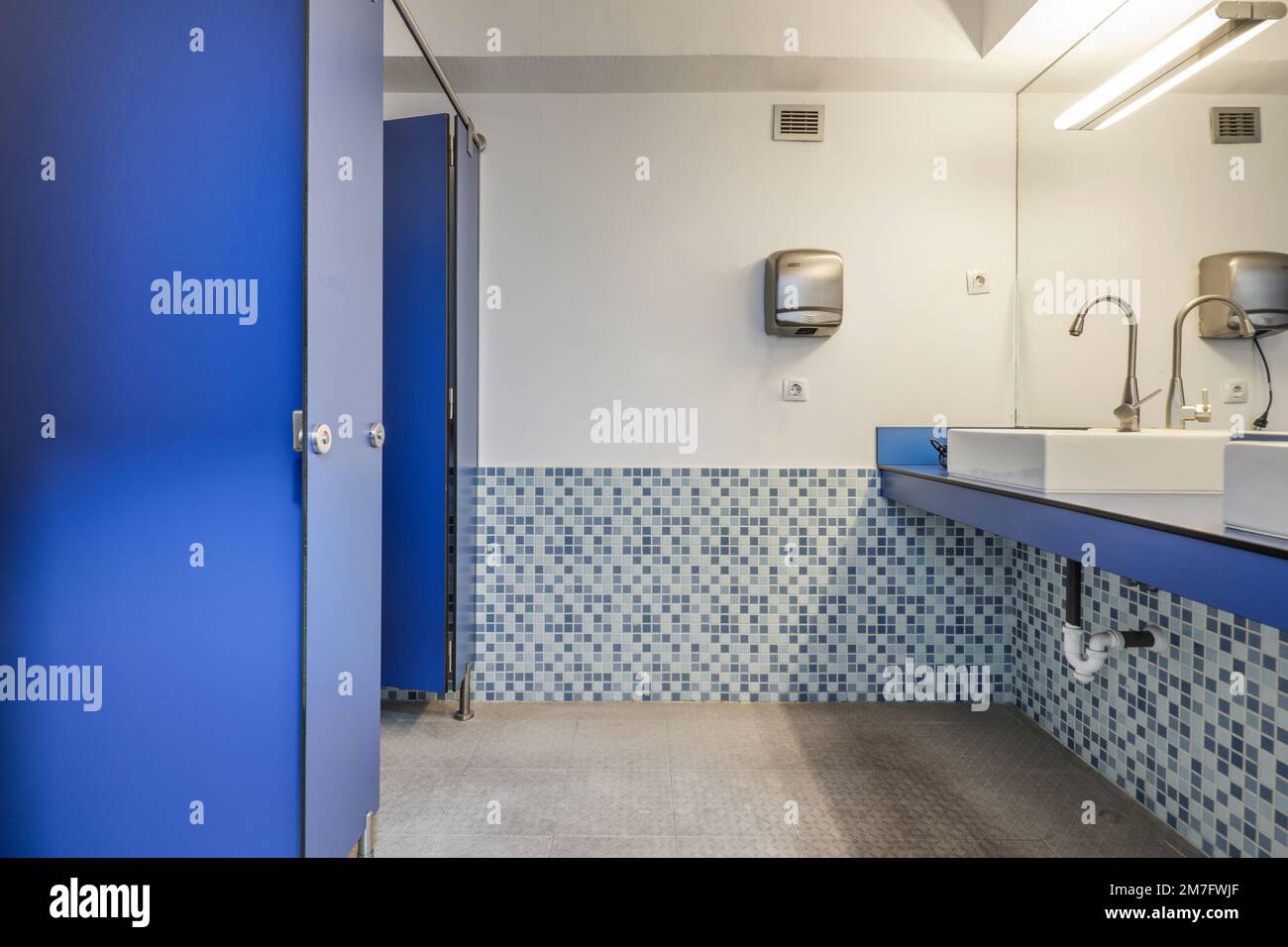 Gym toilet with blue partitions, porcelain sink and blue countertop to ...