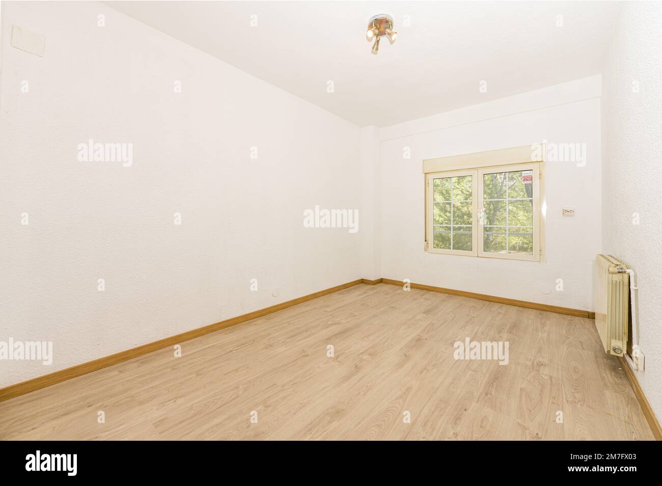 Empty room with light wooden flooring, oak skirting, aluminum radiator ...