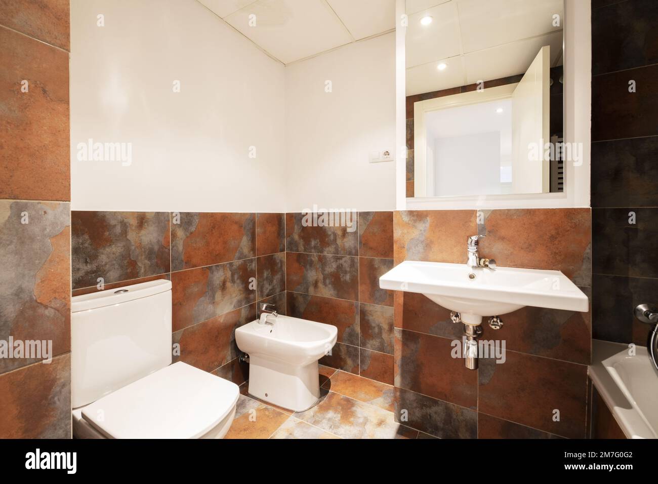 Bathroom with mottled tiled wall, white sanitary ware and rectangular ...