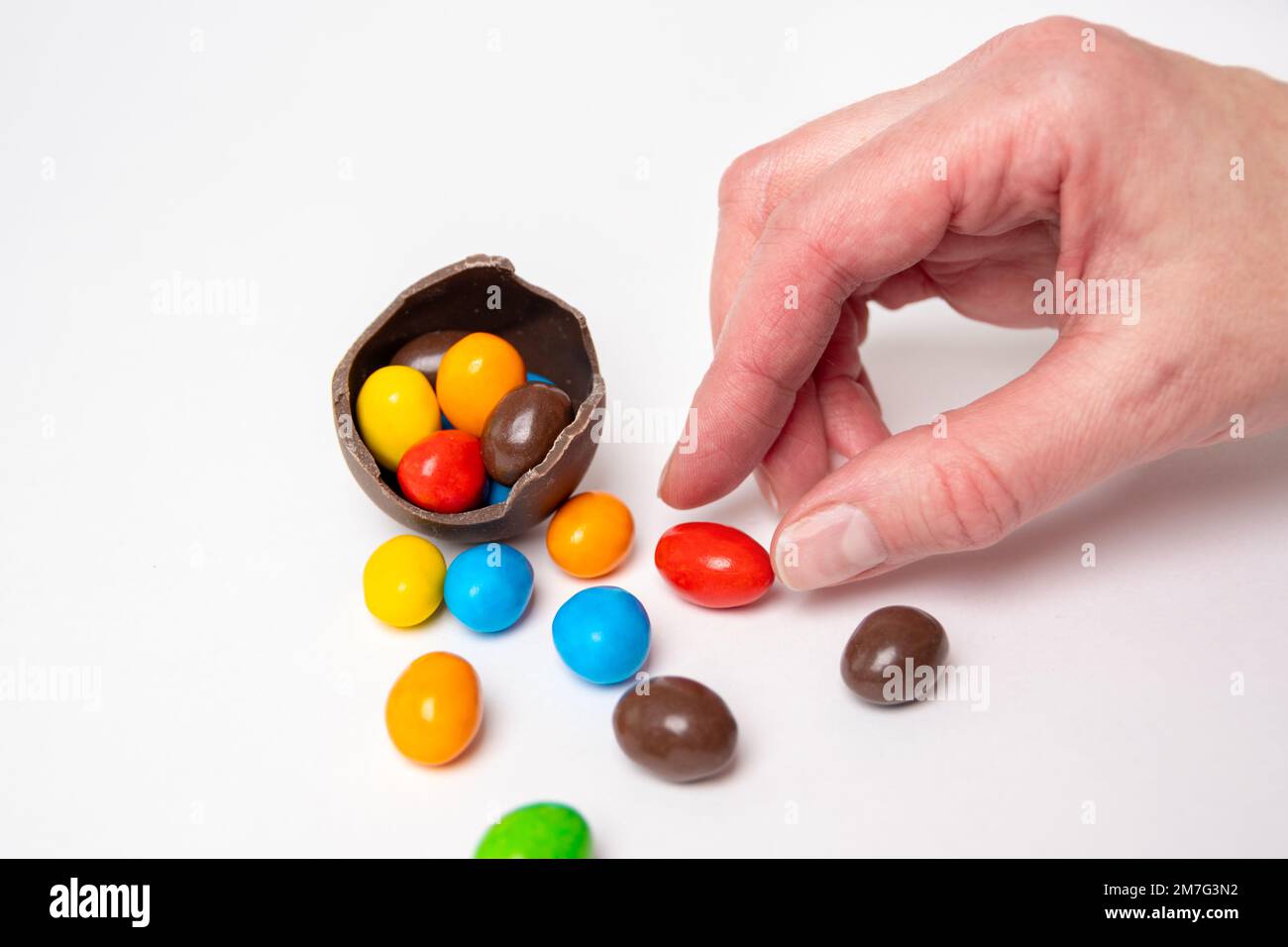 A hand taking a candy from a cracked chocolate easter egg full of ...