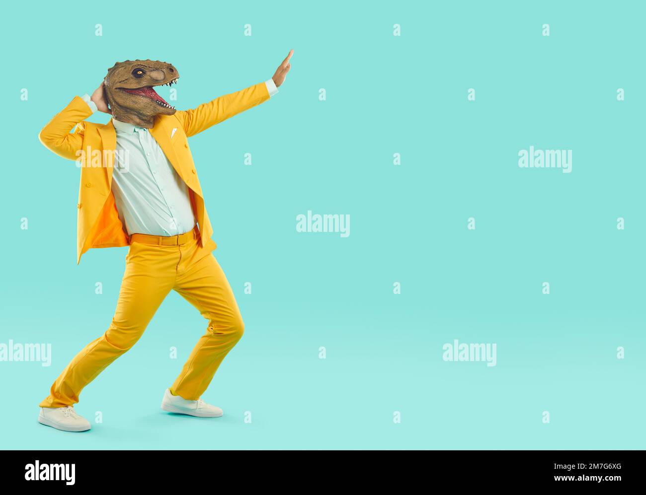 Crazy man in yellow suit and funny dinosaur mask dancing on turquoise ...