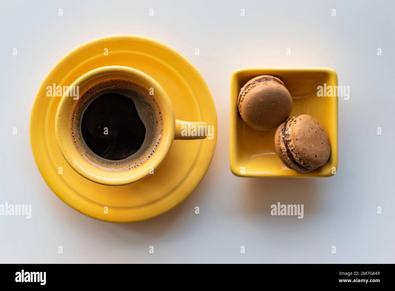 Top angle of a yellow cup of black coffee and two macaroons on white ...