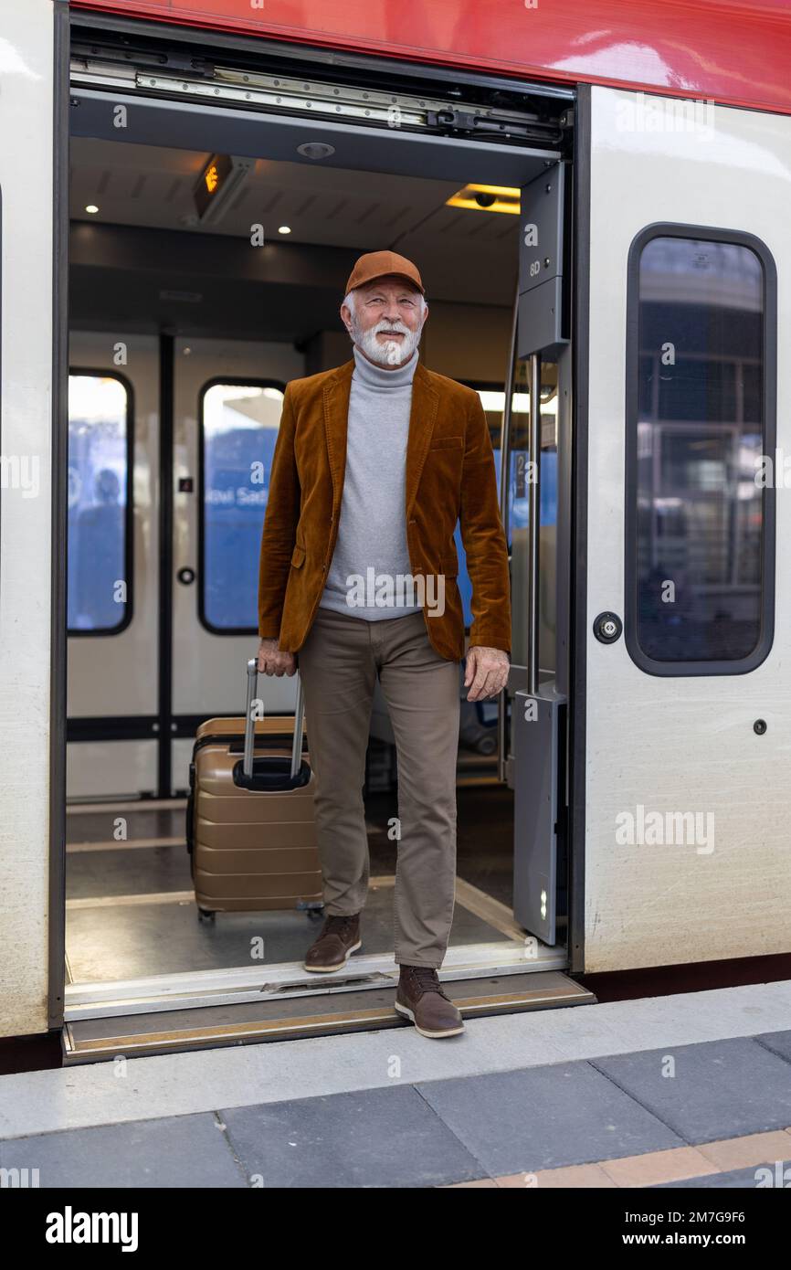 Senior man with suitcase getting out of train on terminal at station ...