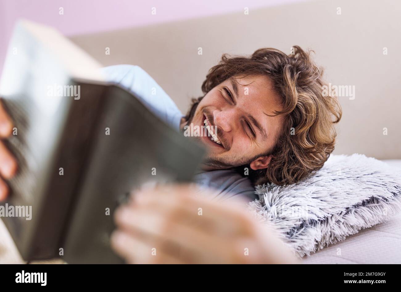 Young man reading interesting book in bad and laughing Stock Photo - Alamy
