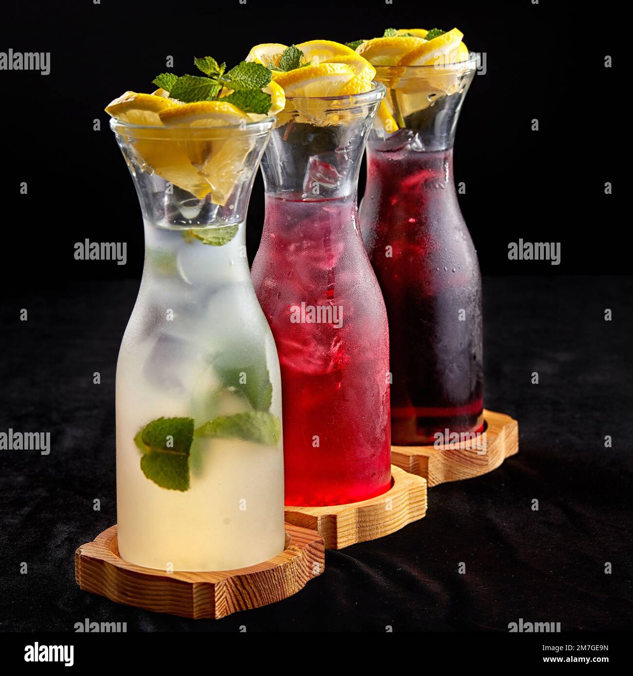 Three different bottles of lemonade, on a wooden board on a black ...
