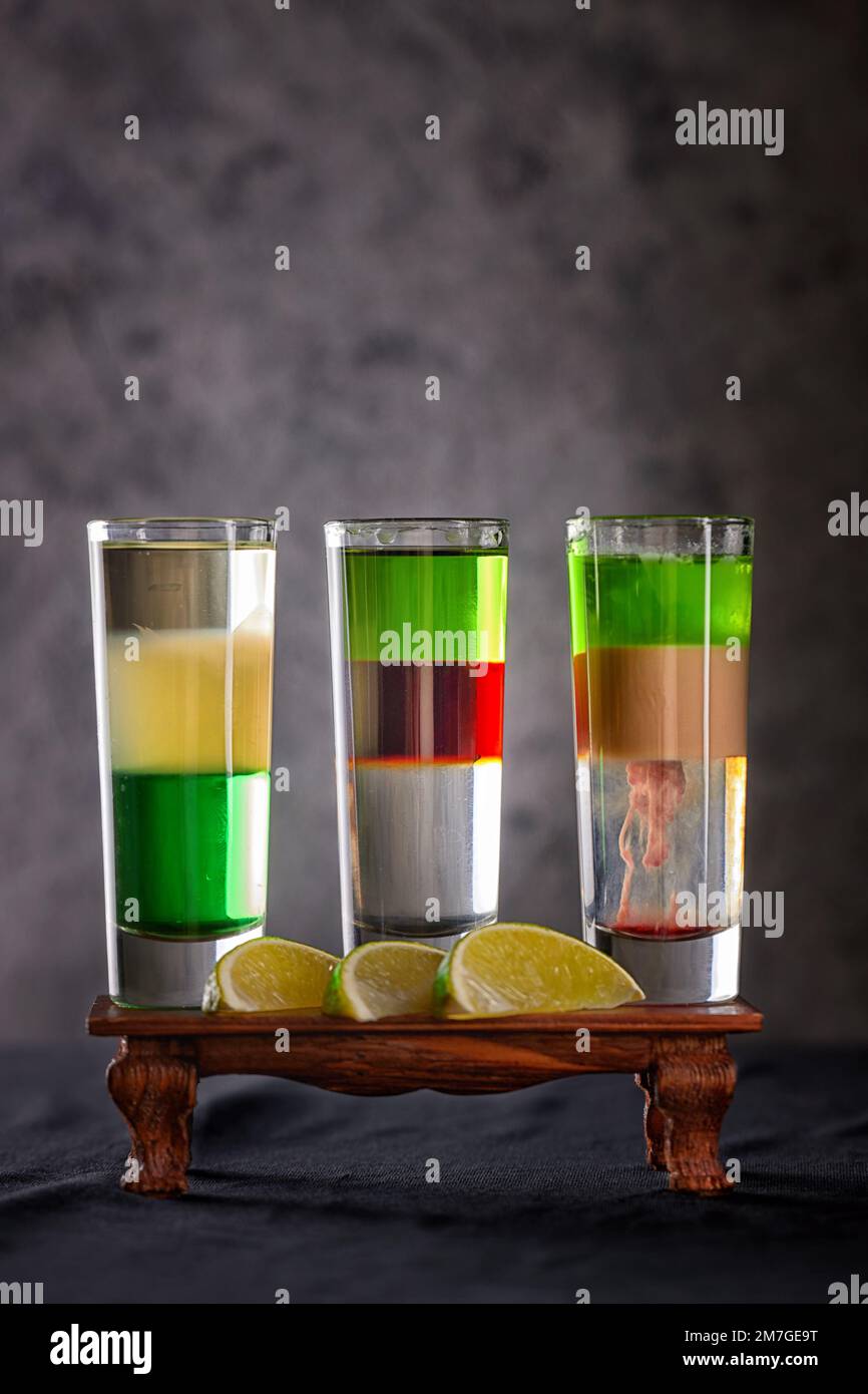 Layered alcoholic cocktails, on a wooden board on a black background ...