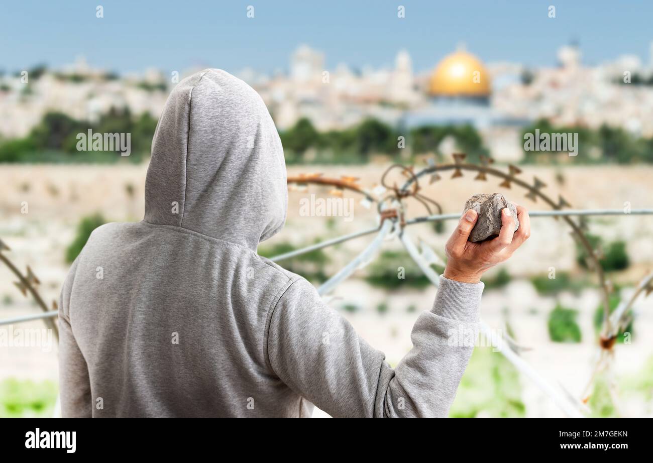 Rear view of a hooded person throwing stones at a metal balla in ...