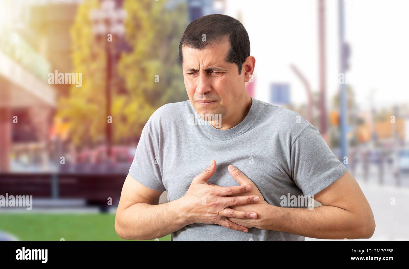 Shot of a man holding his chest in discomfort due to pain in the street ...