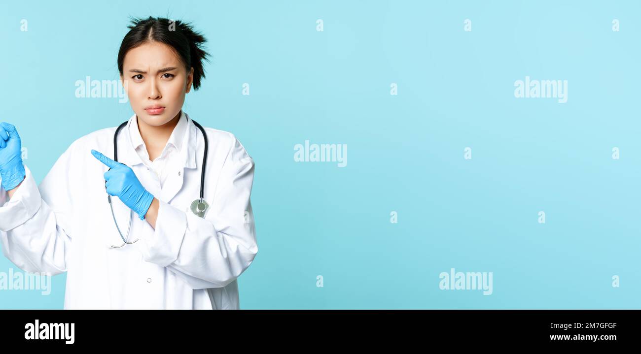 Angry female doctor or nurse, pointing fingers at upper left corner ...