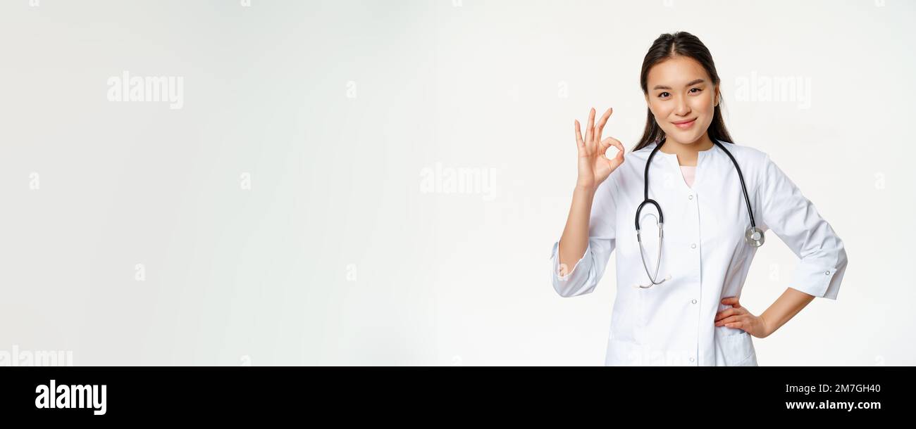 Very good. Smiling confident asian female doctor, showing okay, ok sign ...