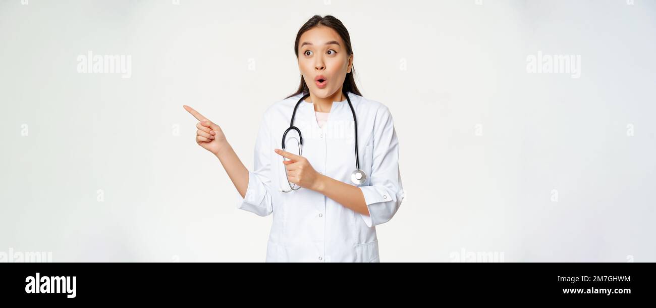 Portrait of enthusiastic female doctor, asian physician pointing and ...