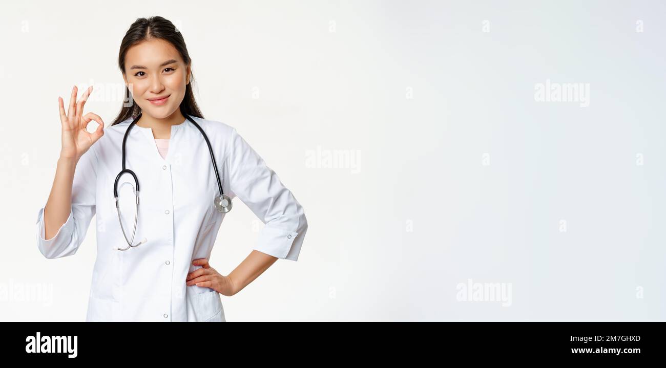 Very good. Smiling confident asian female doctor, showing okay, ok sign ...