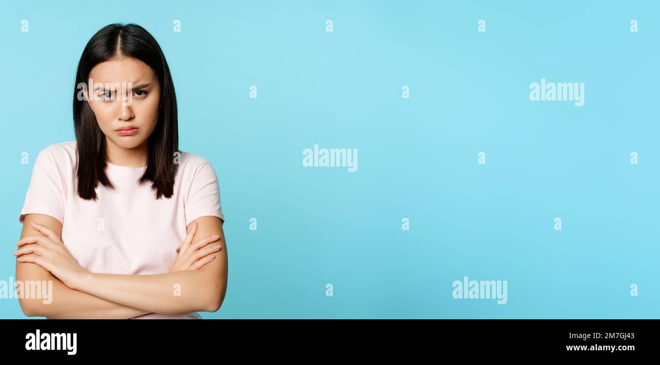 Angry teen asian girl standing in offended pose, frowning and sulking ...