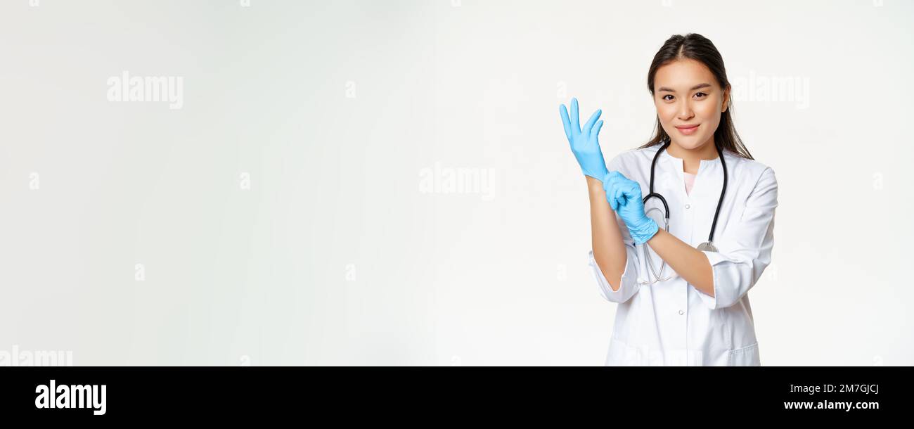 Smiling confident asian female doctor put on medical gloves, getting ...