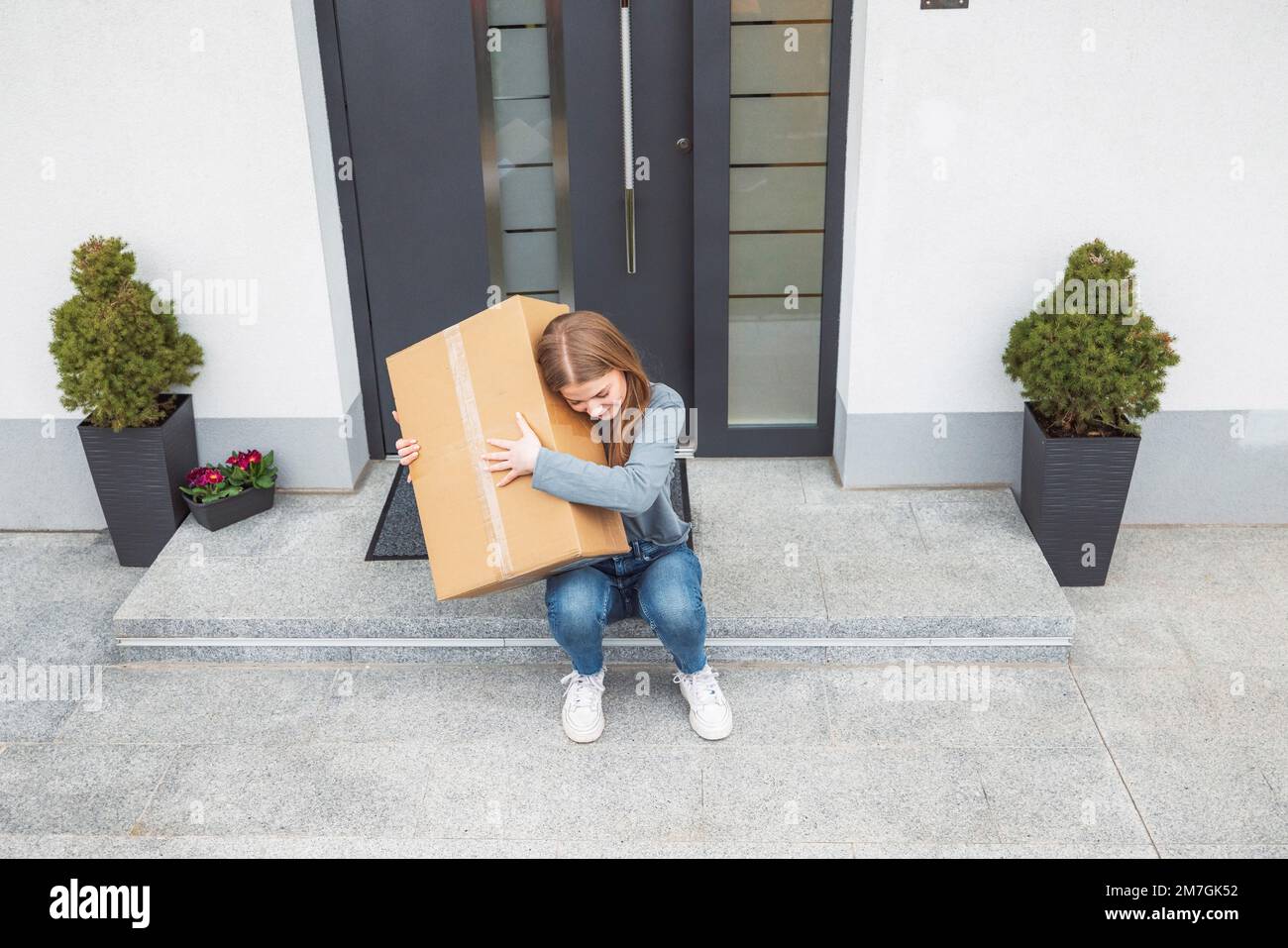 Caucasian woman sitting down on a step at the front door of the house ...