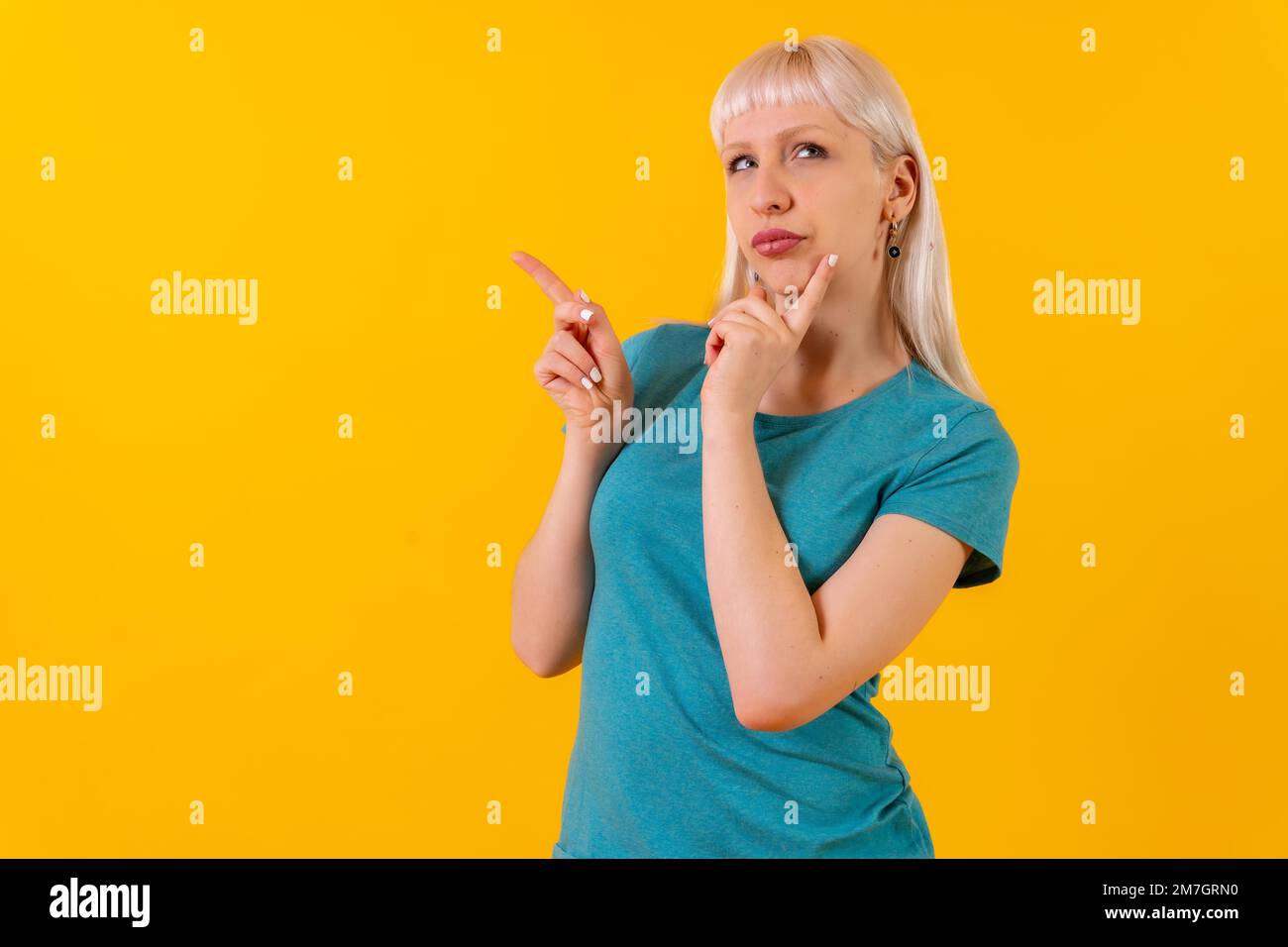 Portrait with pensive pointing posture, blonde caucasian girl in studio ...