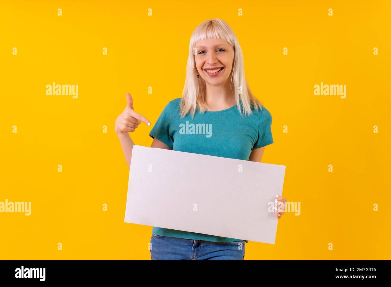 Pointing at white empty advertisement poster, blonde caucasian girl on ...