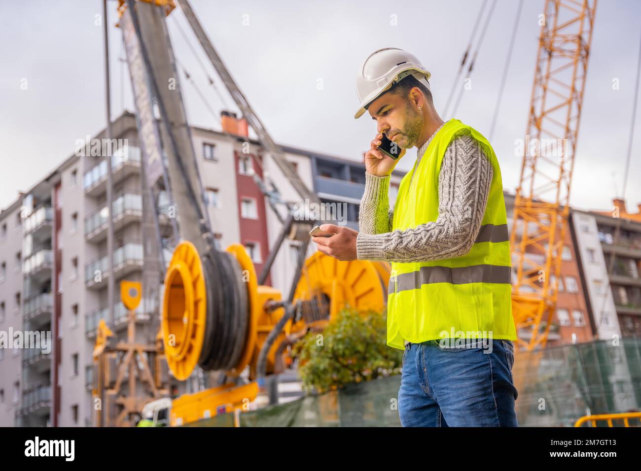 Site manager and technical engineer observing the city construction site, talking on the phone ...