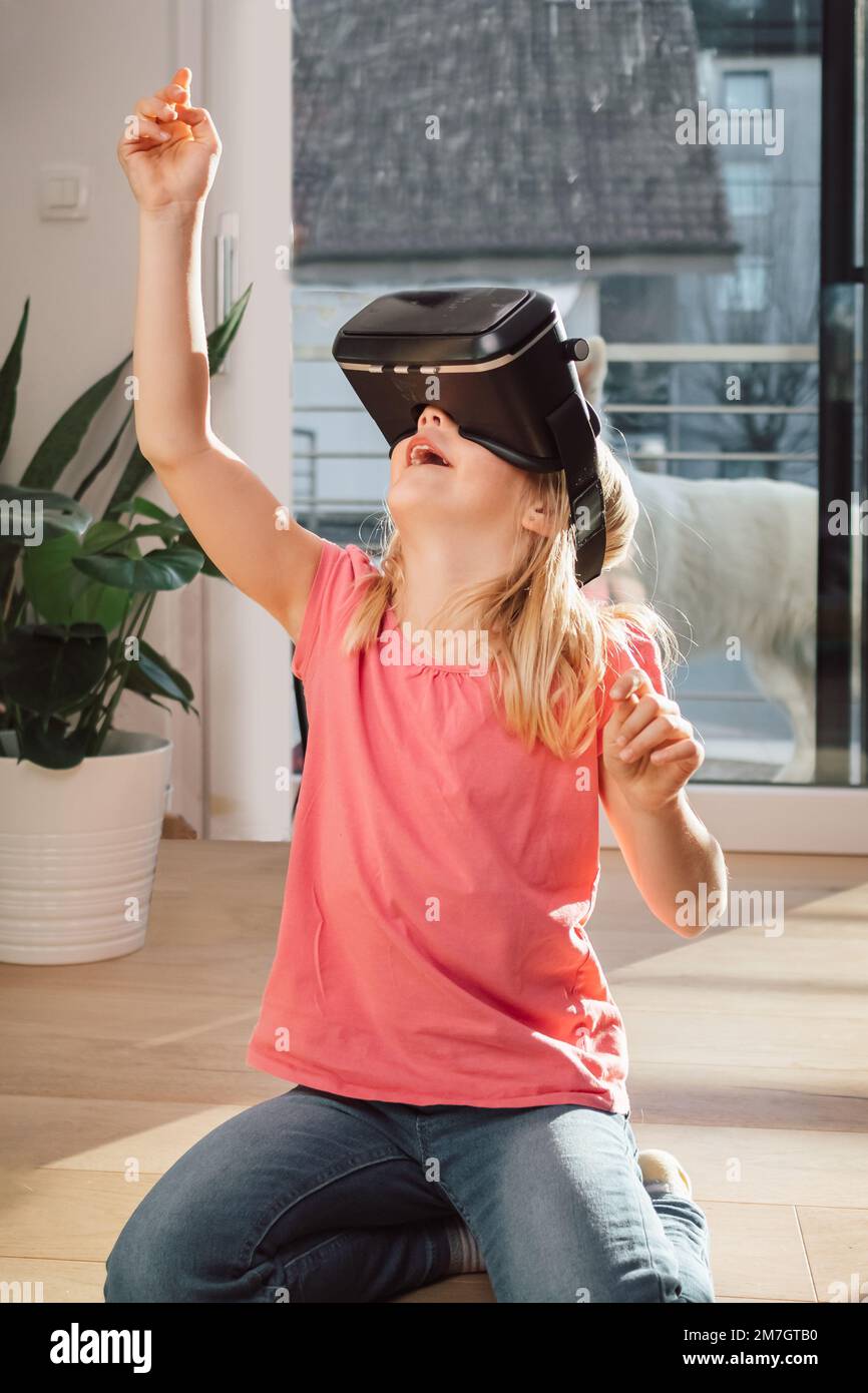 Cute Caucasian female child using VR goggles and playing in imagination world, gesturing with ...
