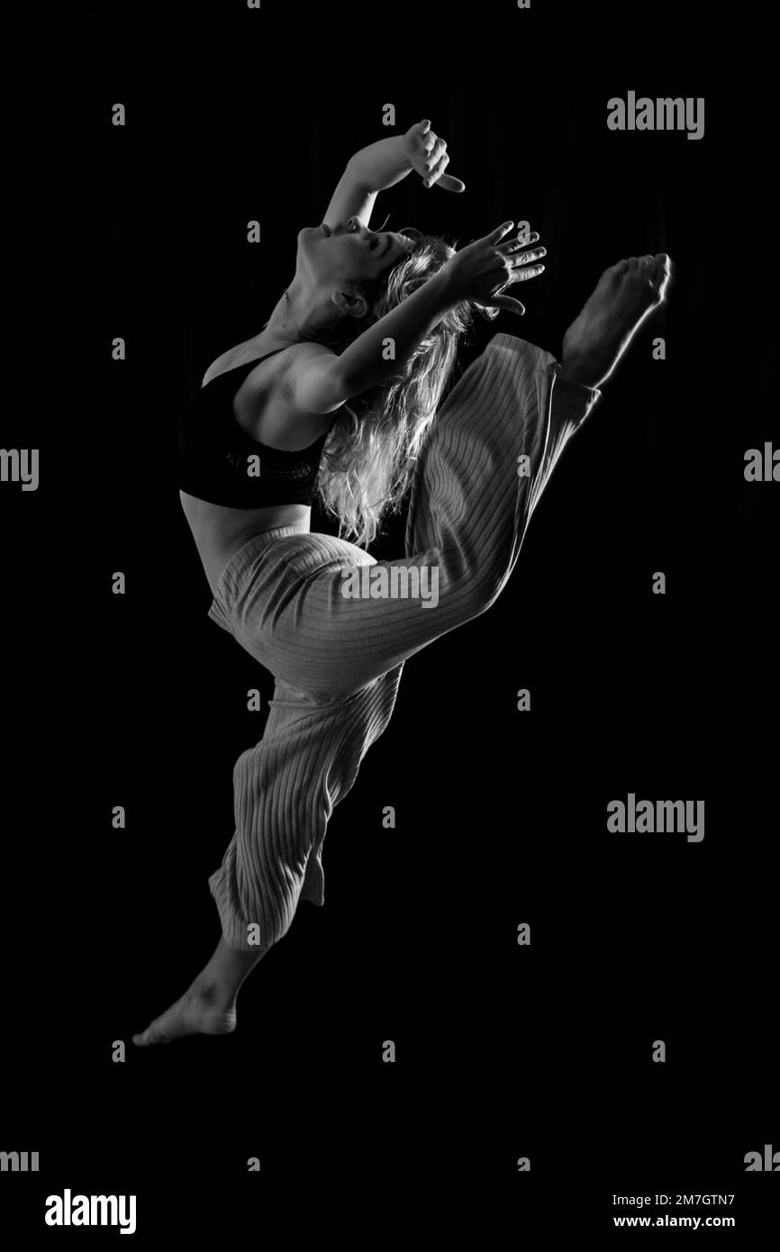 Young dancer in studio photo session with a black background, ballet, performing a jump in black ...