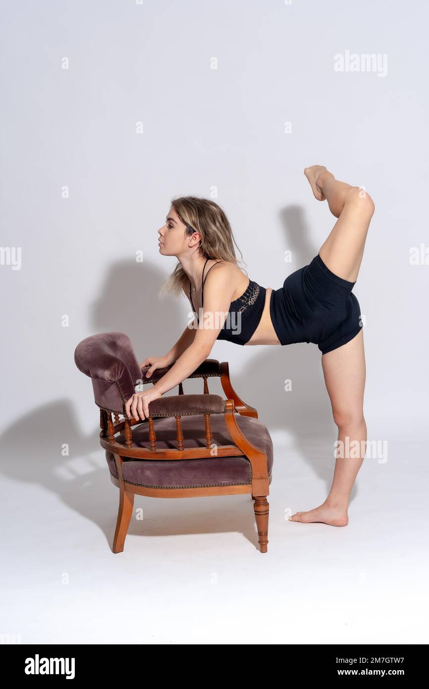 Young dancer on a white background, ballet, raising her leg on a sofa ...