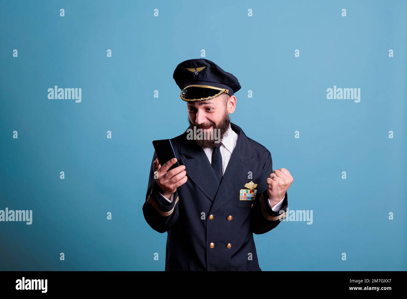 Happy excited airplane captain in uniform holding smartphone with ...