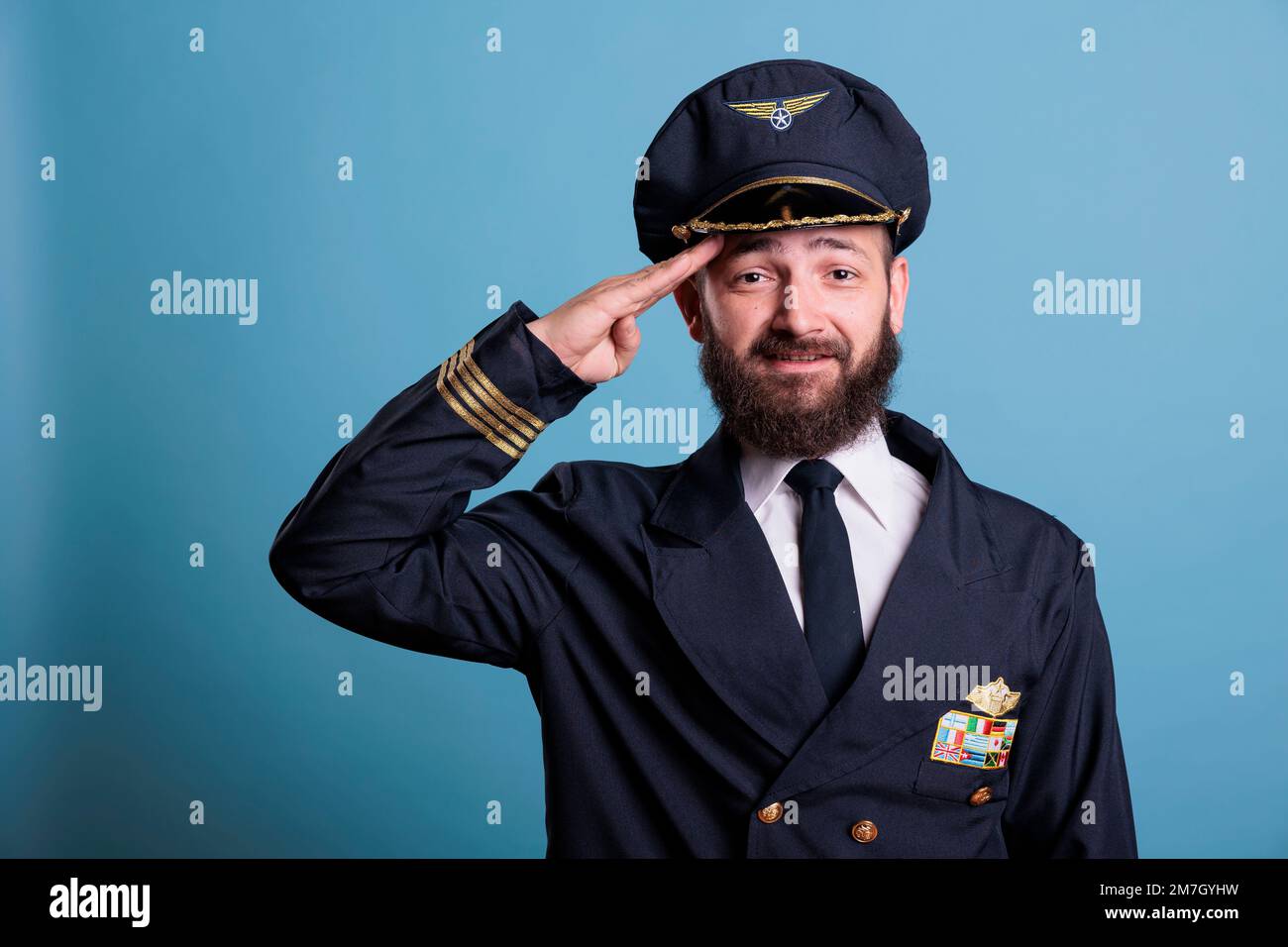 Smiling airplane captain saluting, wearing aviation uniform and hat ...