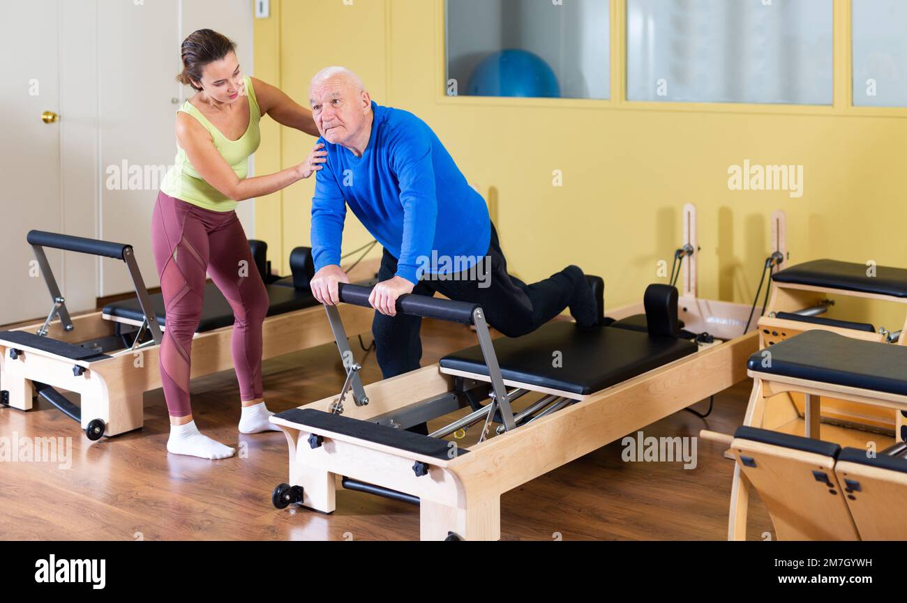 Female trainer controlling senior man doing pilates on reformer Stock ...