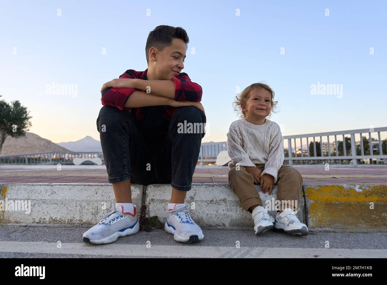 Two brothers sitting outside on a sidewalk and have fun Stock Photo - Alamy