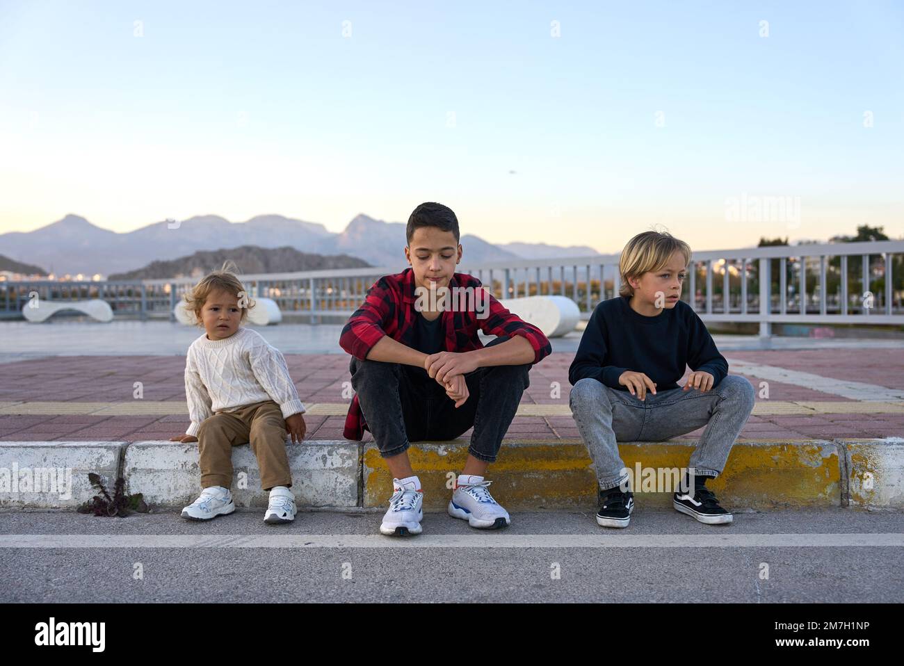 Three brothers sitting outside on a sidewalk and have fun Stock Photo ...