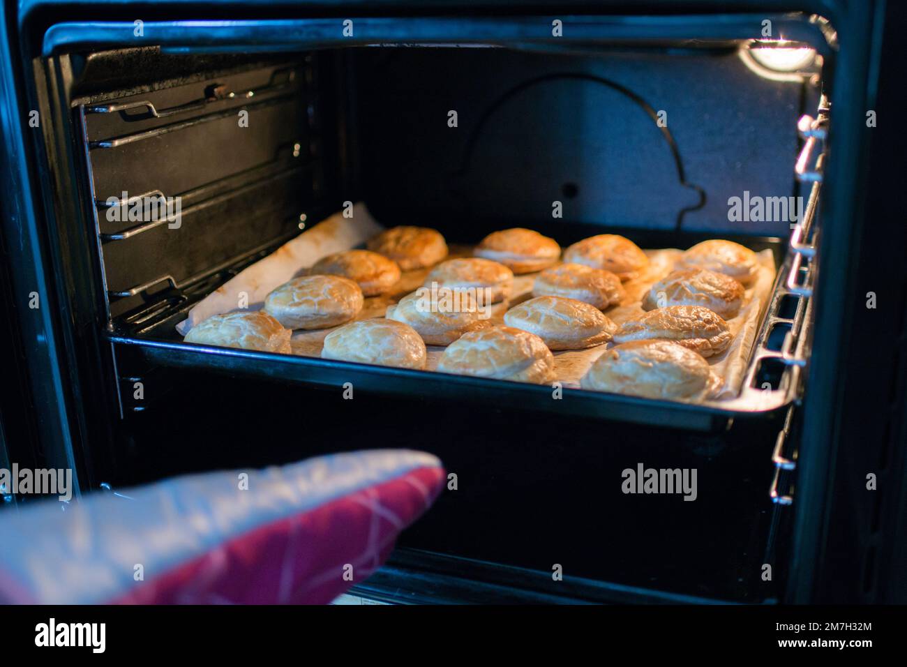 Human hand with an oven glove taking out of the oven a tray with pastry ...