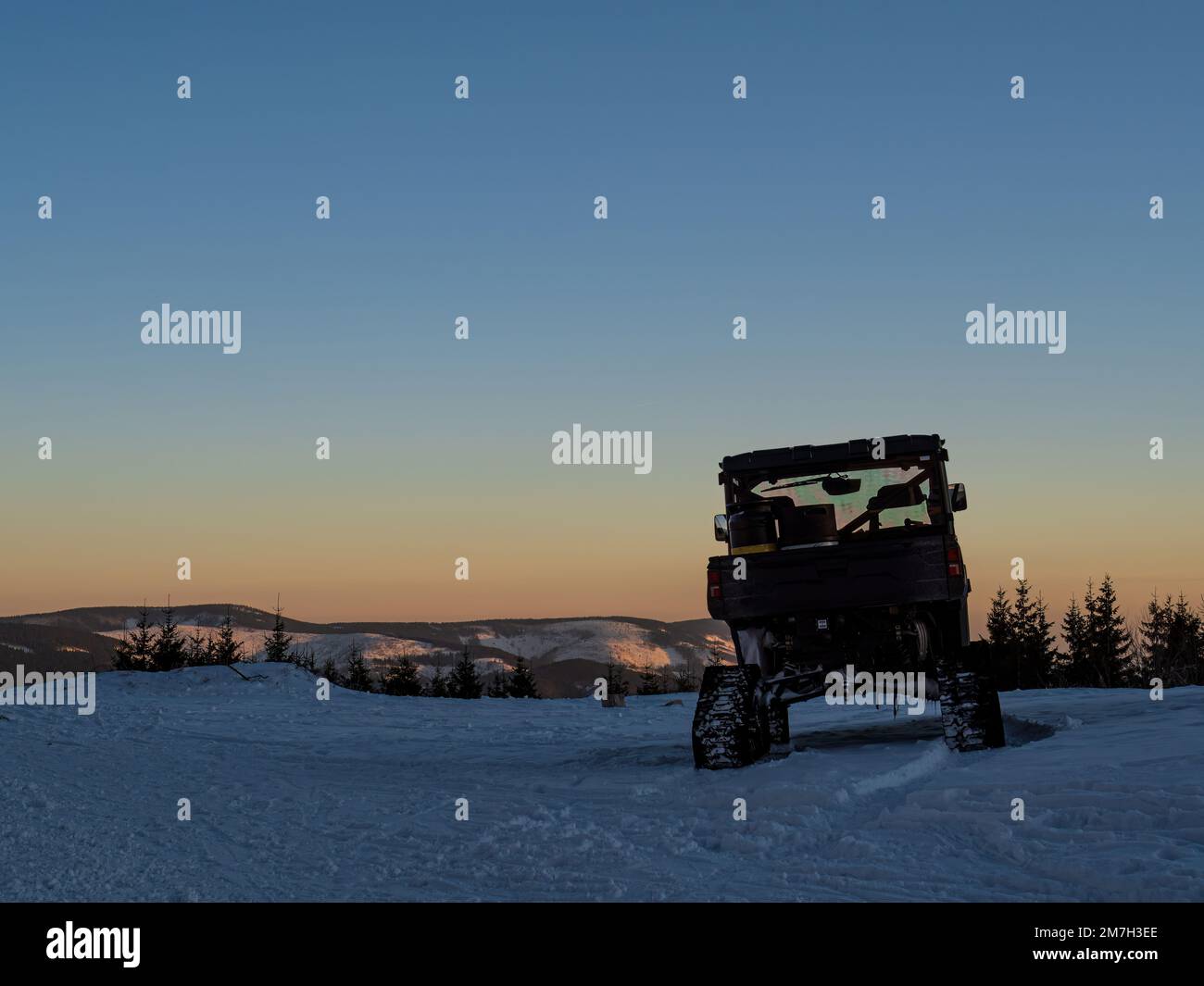 Tracked electric UTV snowmobile on a mountaintop during sunset winter ...