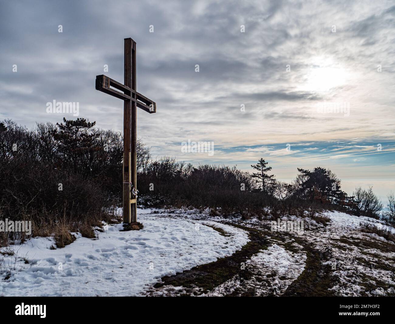Wooden cross standing on a snowy mountaintop winter cloudy sky with sun ...