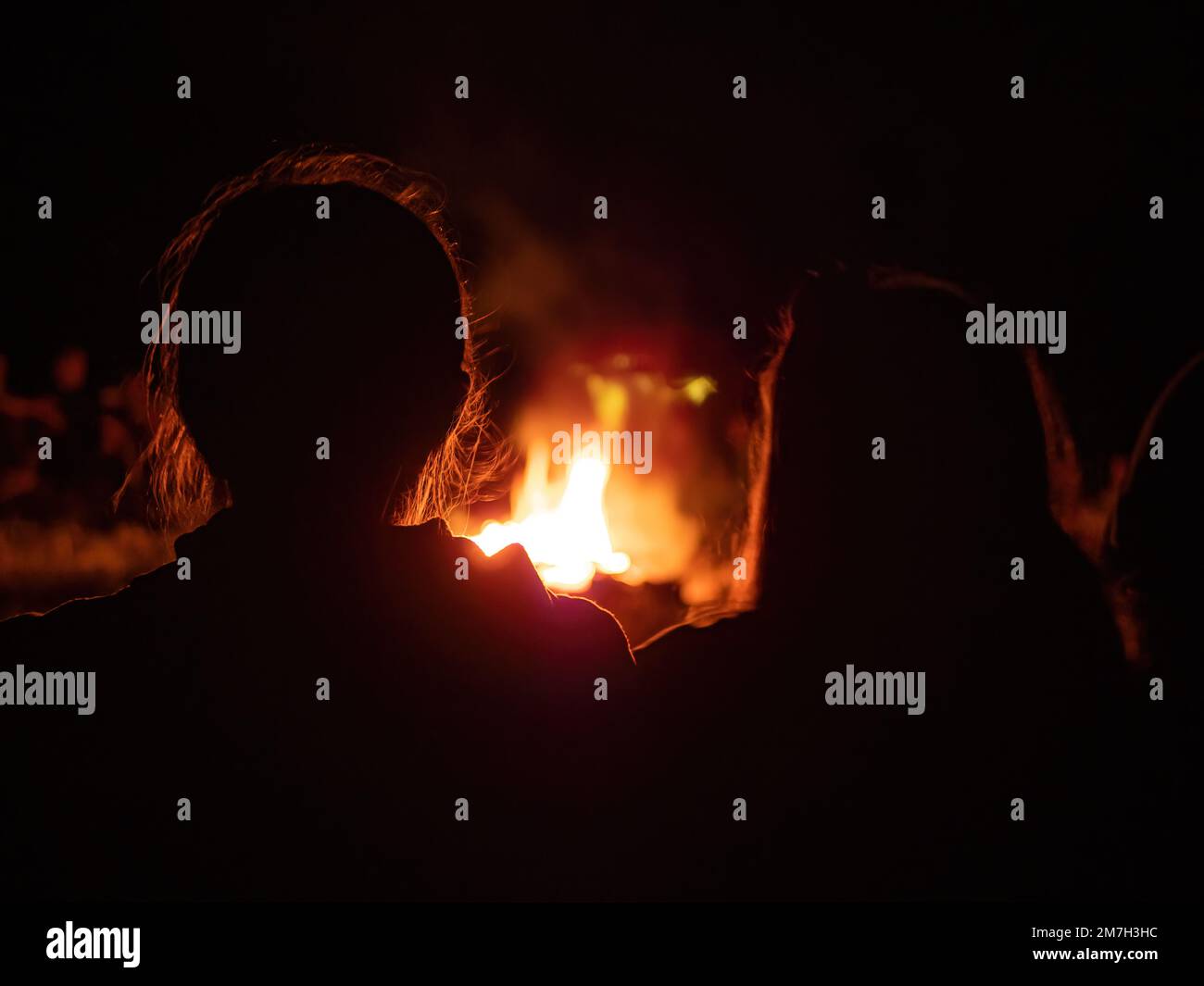 Two girls young woman silhouette from the back sitting at a campfire ...