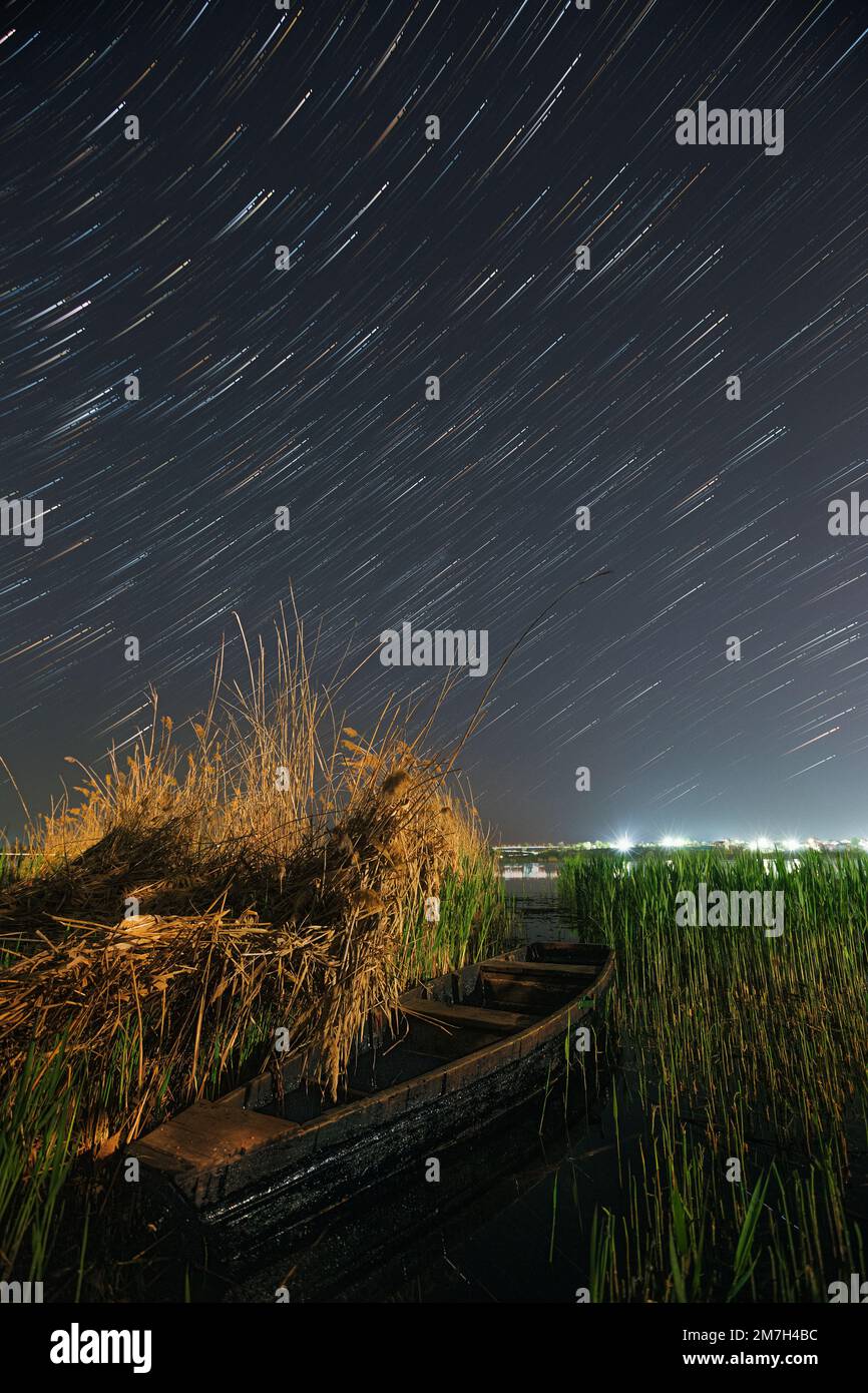Night cosmic star trails landscape with boat floating on a river's ...