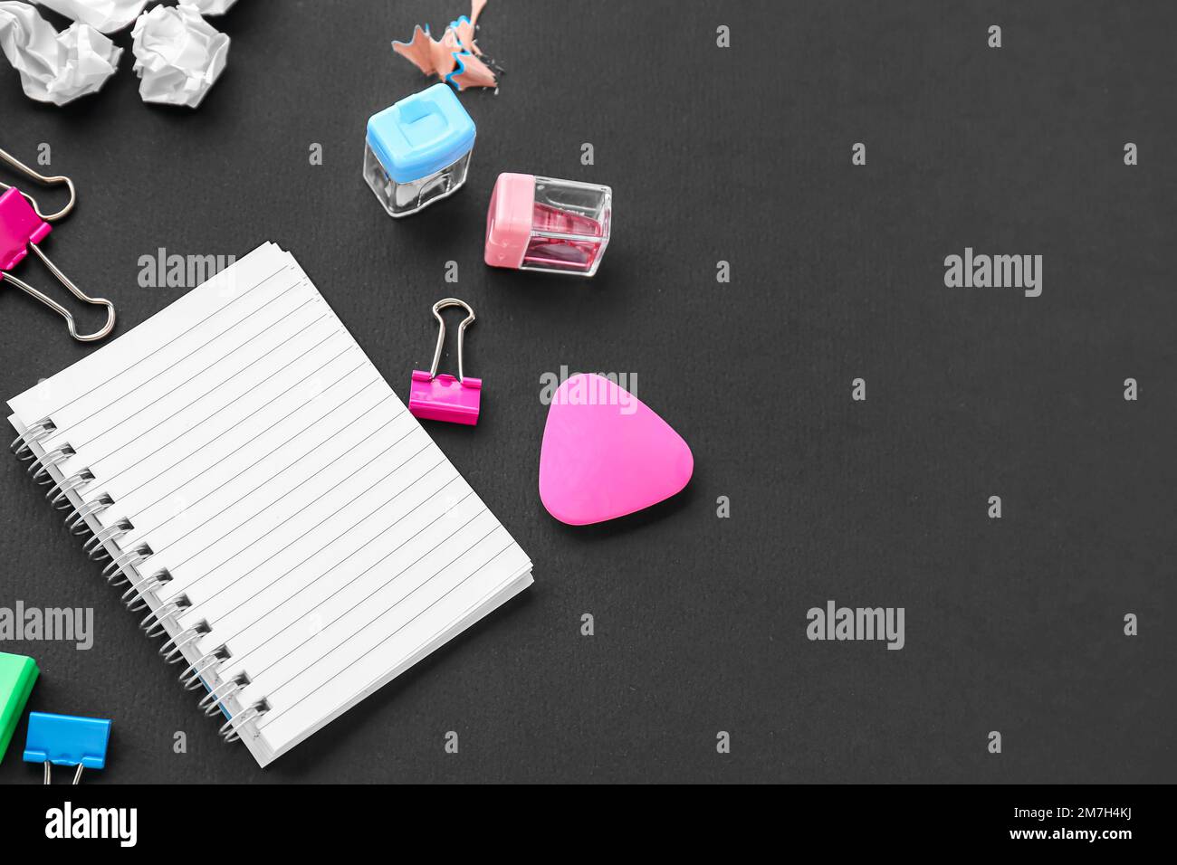Blank notebook, binder clips, eraser and sharpeners on dark background ...