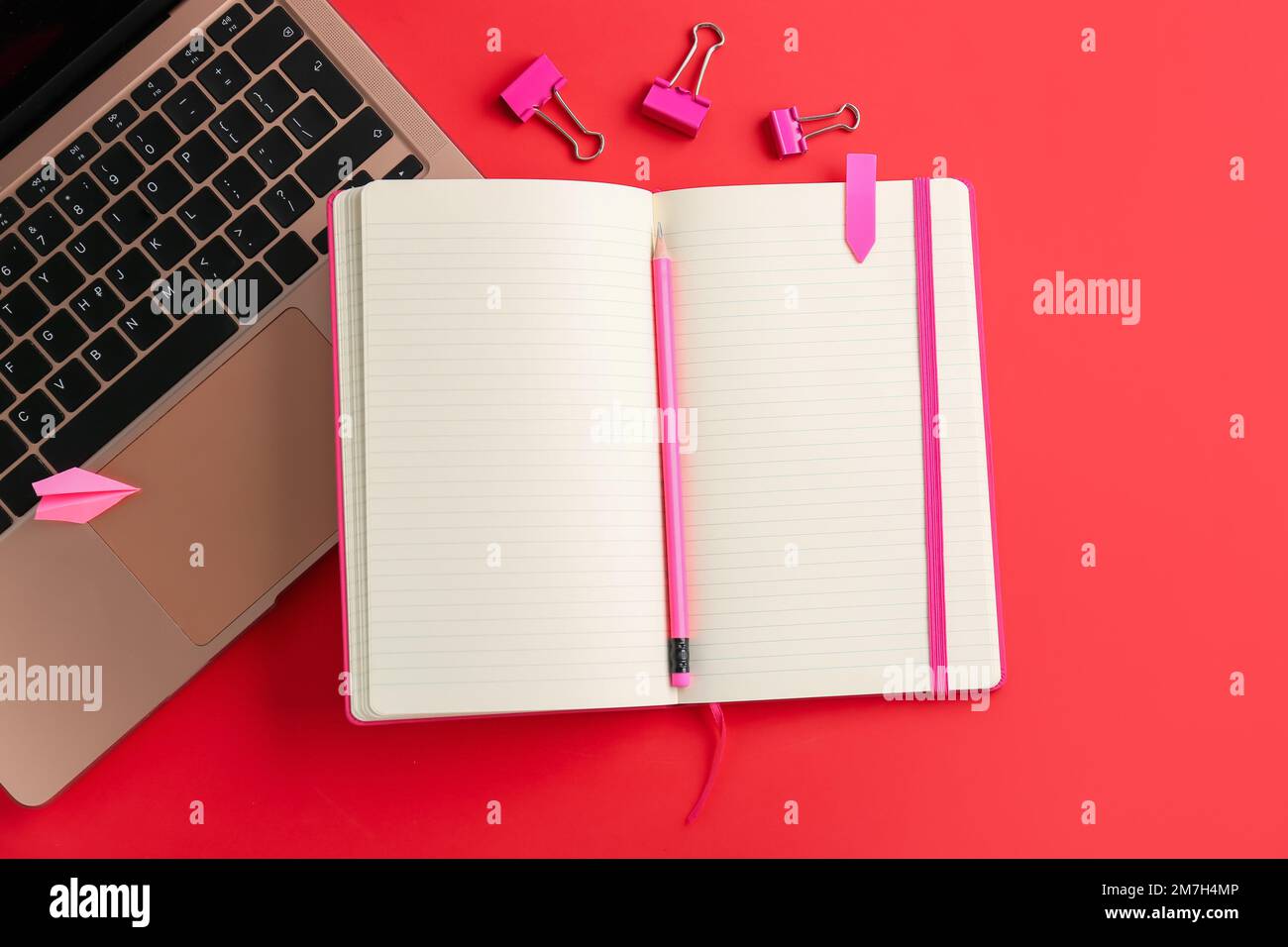 Open notebook, pencil, binder clips and laptop on red background Stock ...