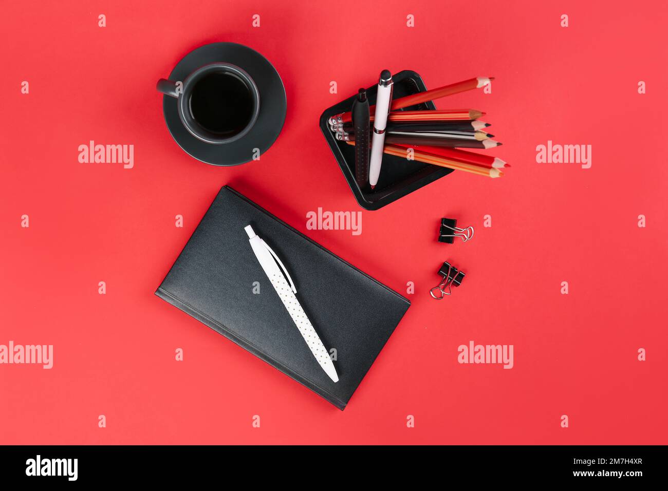 Notebook, stationery holder, paperclips and cup on red background Stock ...