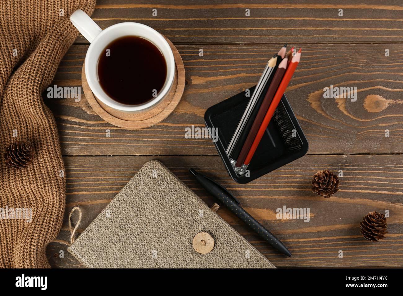 Notebook, holder with stationery, cup of coffee and pine cones on ...
