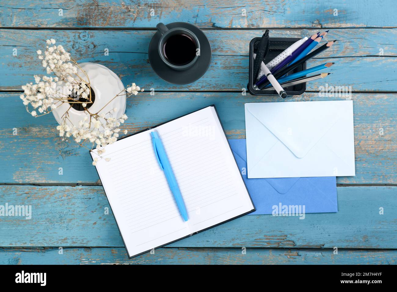 Notebook, holder with stationery, cup of coffee and vase with flowers ...