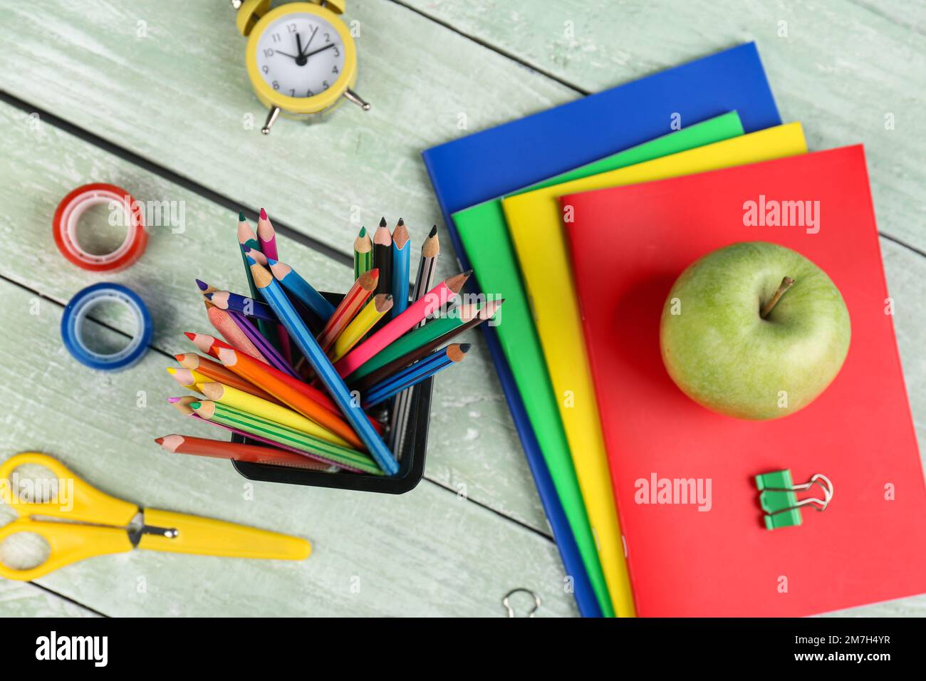 Green apple with notebooks, pencils holder, school stationery and clock ...