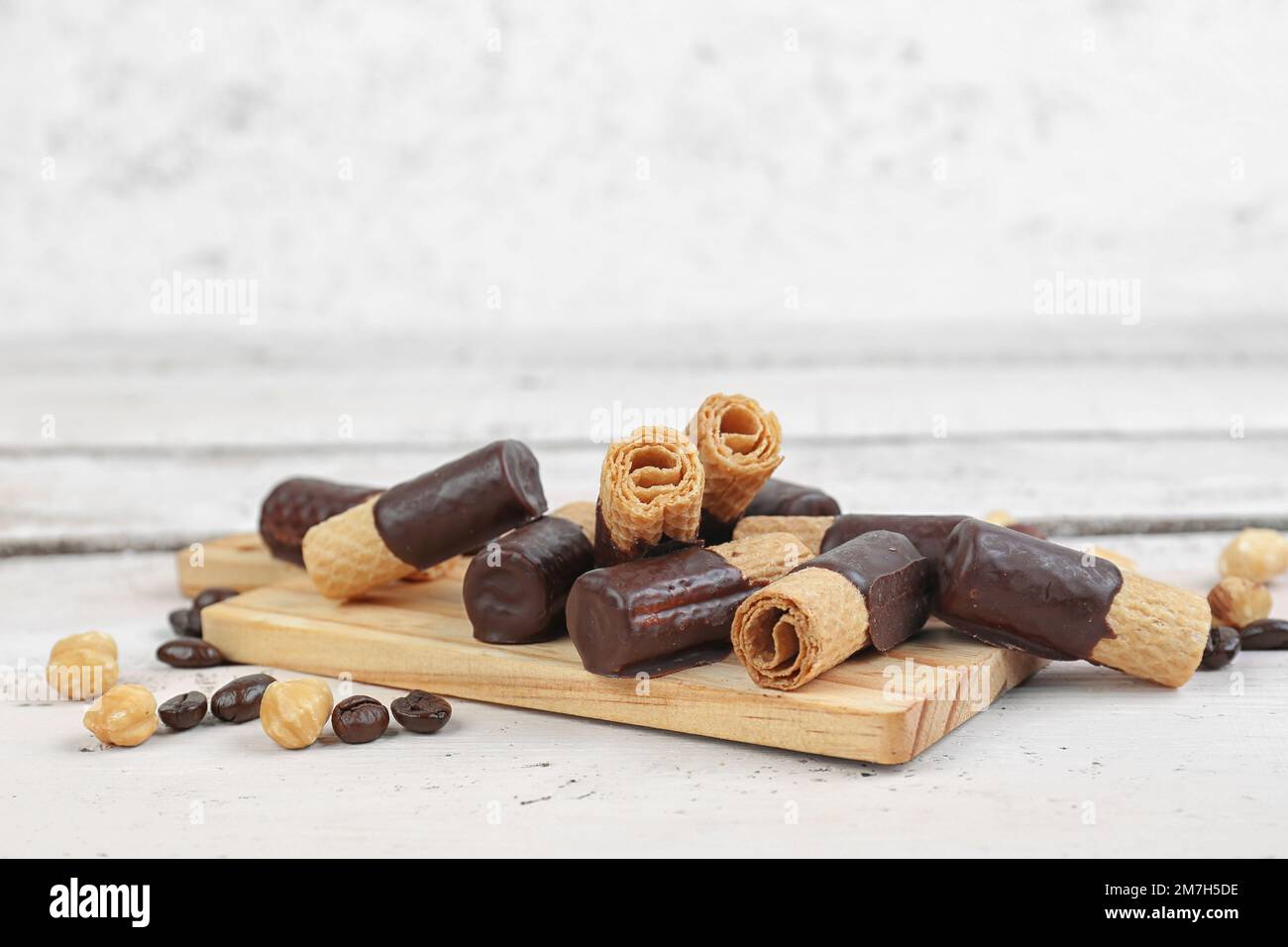 Cutting board with heap of delicious wafer rolls, coffee beans and nuts ...