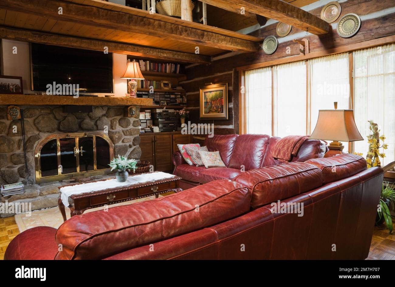 Burgundy leather sofas and fireplace in family room inside reconstructed 1800s cottage style log ...