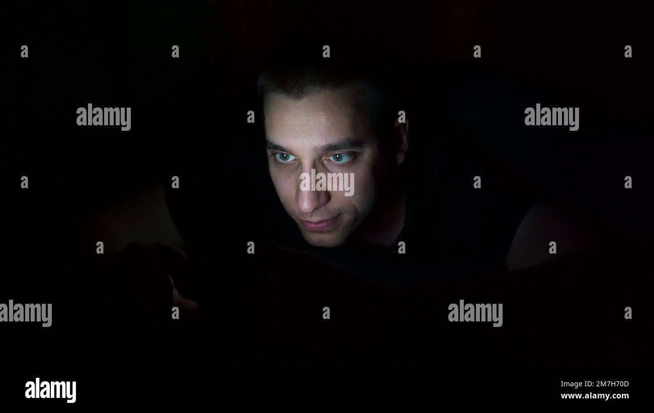 young guy looks at the phone before going to bed at night. Examines ...