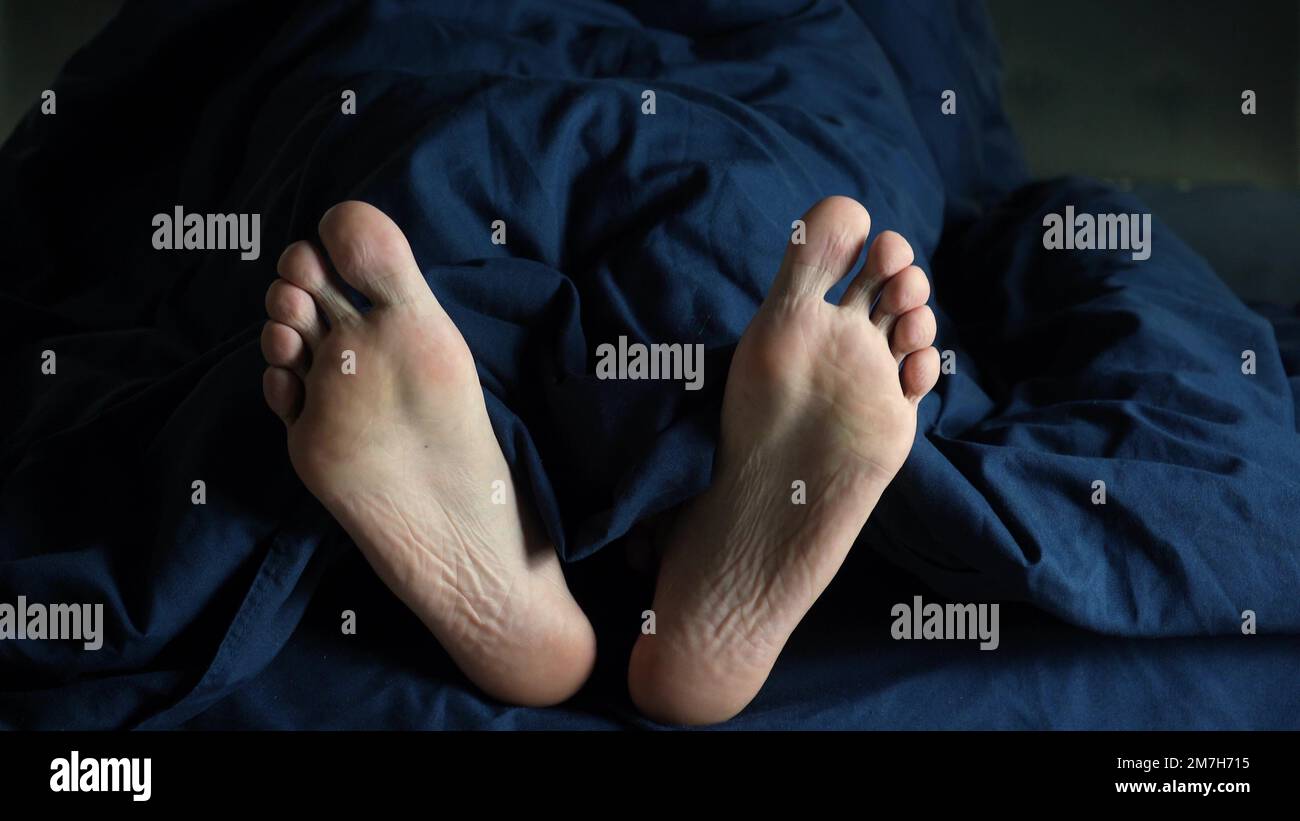 Feet in bed under the covers close-up. Scratches leg on leg. Flexion of ...