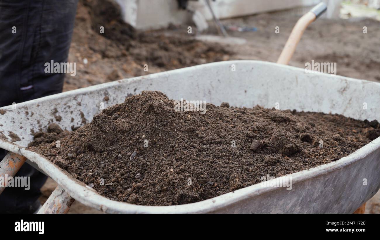 A worker pours soil into a wheelbarrow with a shovel close-up 4K ...