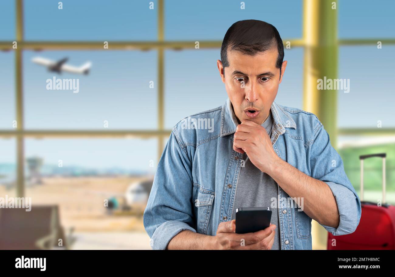 Handsome man using smartphone standing at airport serious face thinking ...