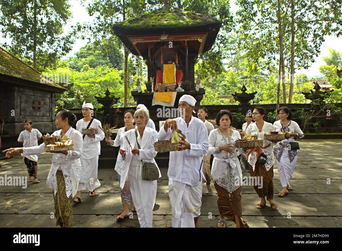 A Balinese priest is standing in front of women of a clan who are ...