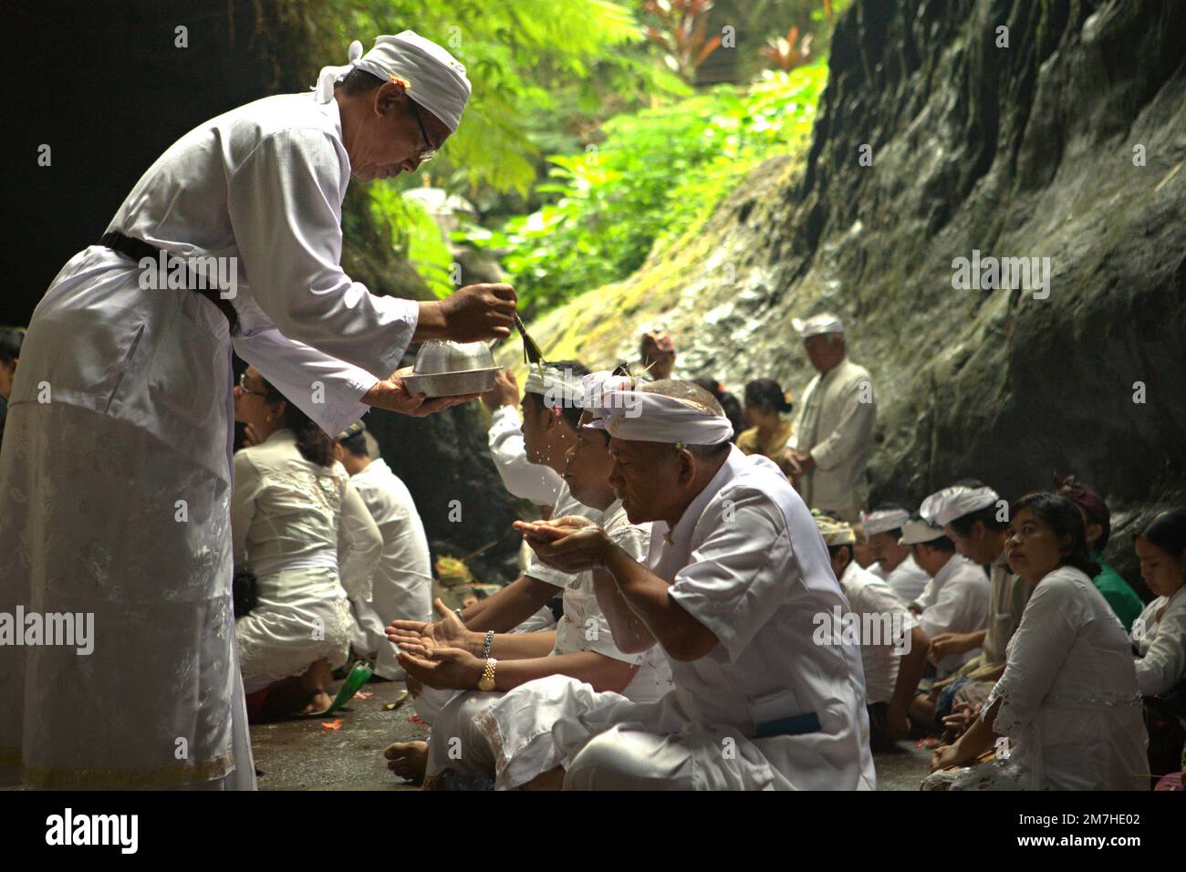 A Balinese Hindu priest is splashing people with water during a ritual ...